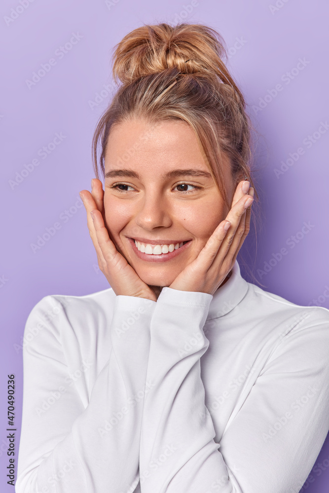 Vertical shot of pretty young woman keeps hands on cheeks smiles gently ...