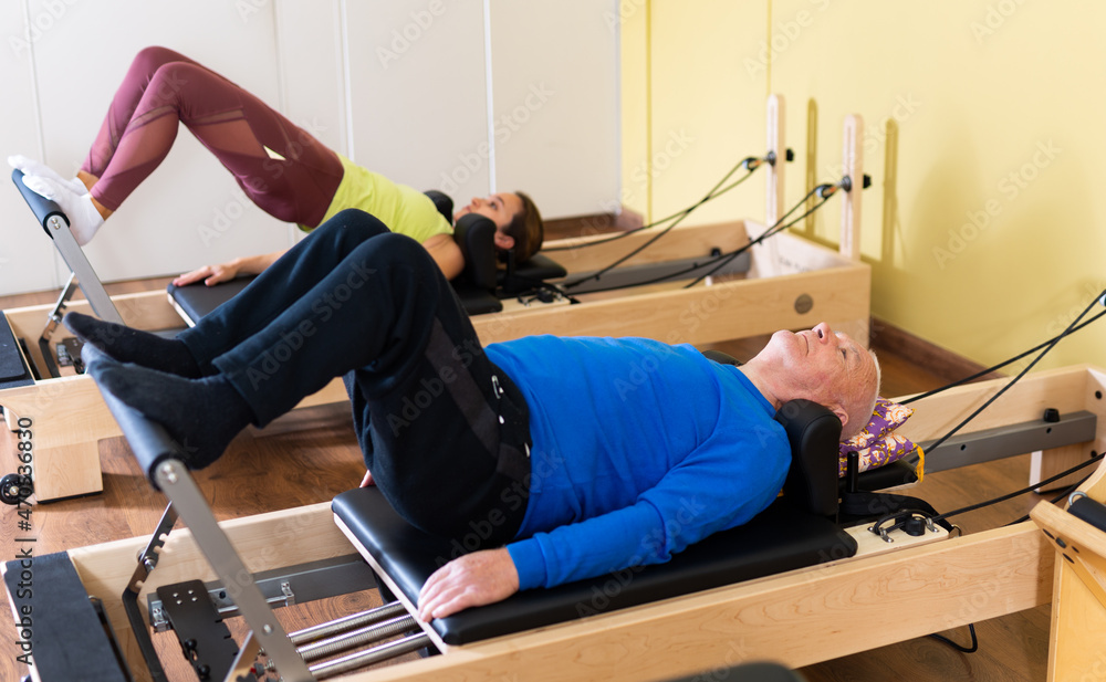 Portrait of elderly man performing set of pilates exercises on reformer ...