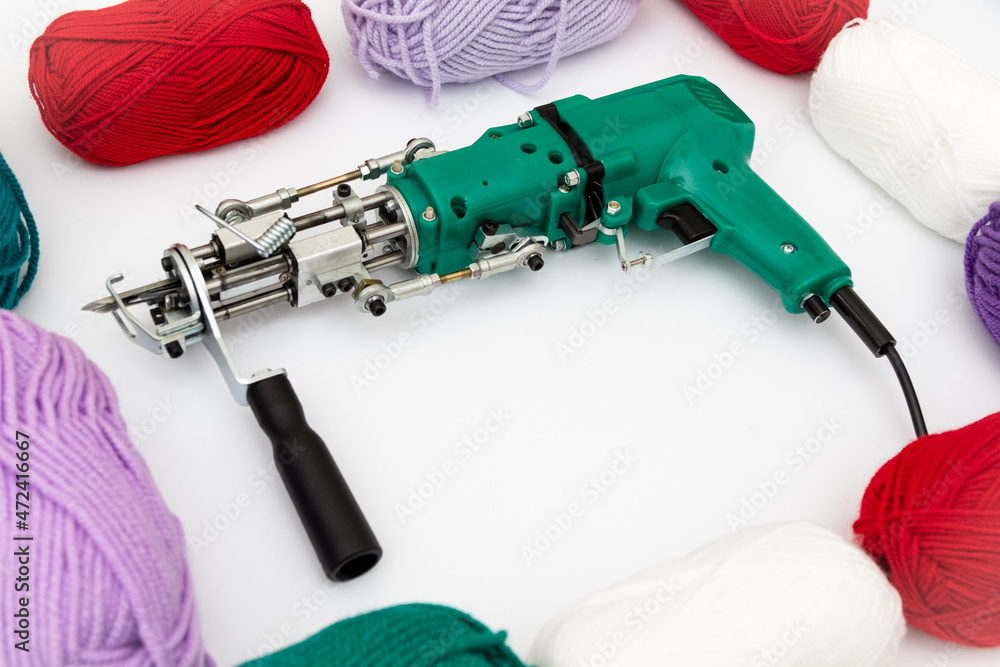 Tufting gun and skeins of yarn of various colors on white background ...