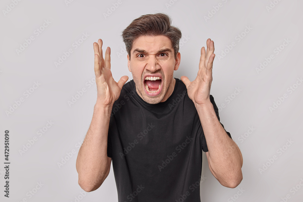 Outraged young man yells angrily keeps mouth opened raises hands being ...