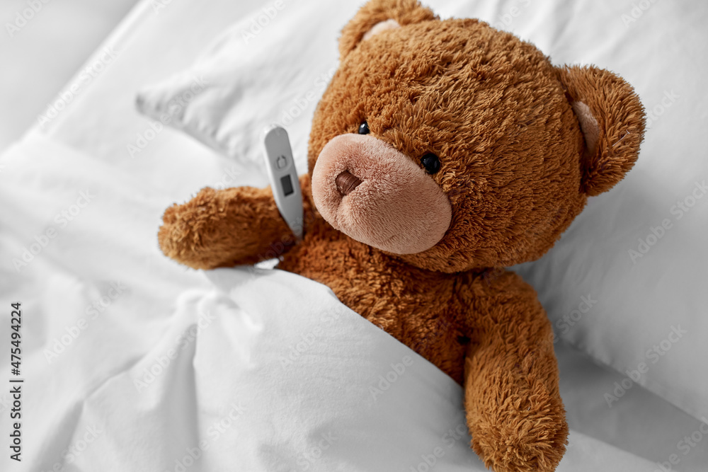 medicine, healthcare and childhood concept - ill teddy bear toy head with thermometer lying in ...