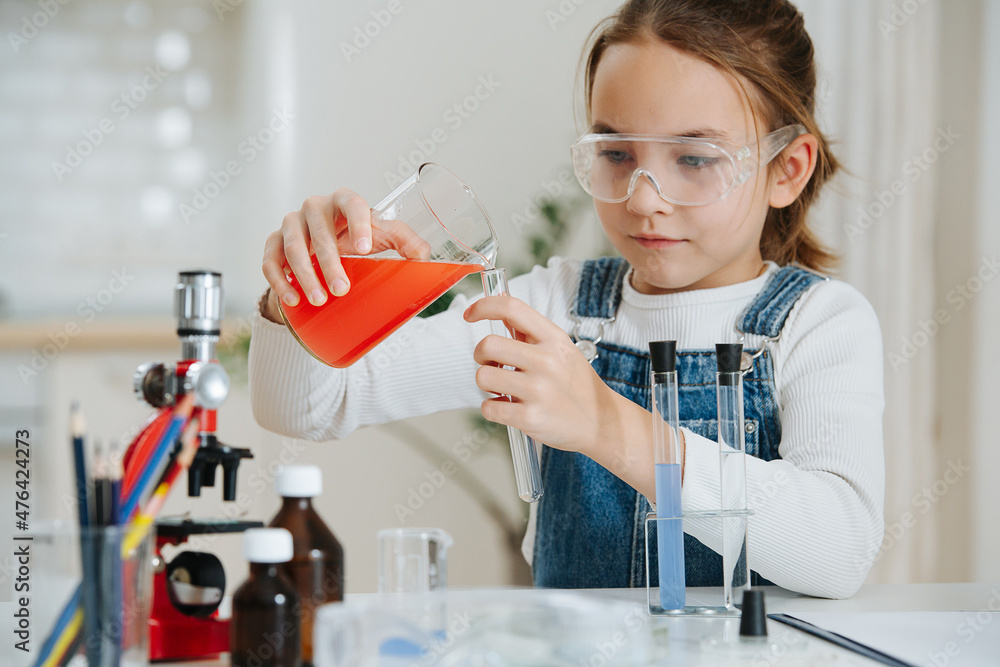 Calm little girl doing home science project, pouring red liquid into a ...