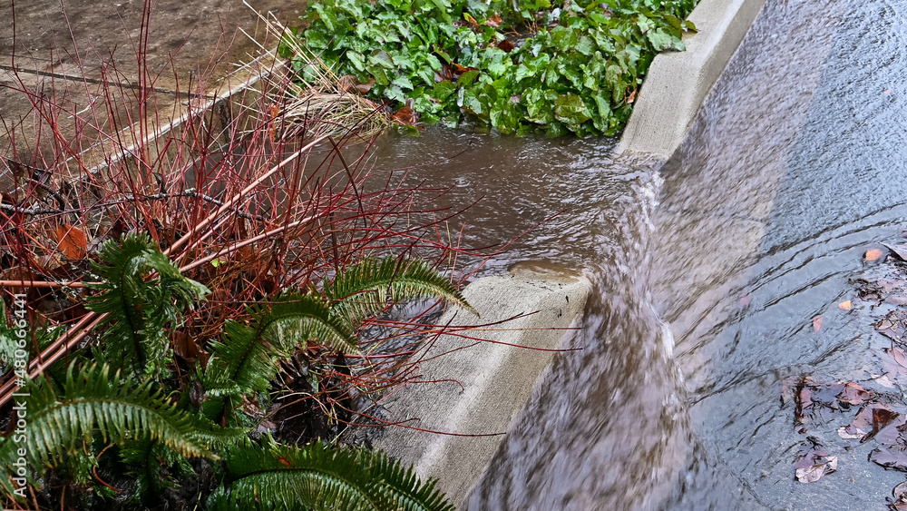 Rainwater flooding down a residential street and flood control ditch ...