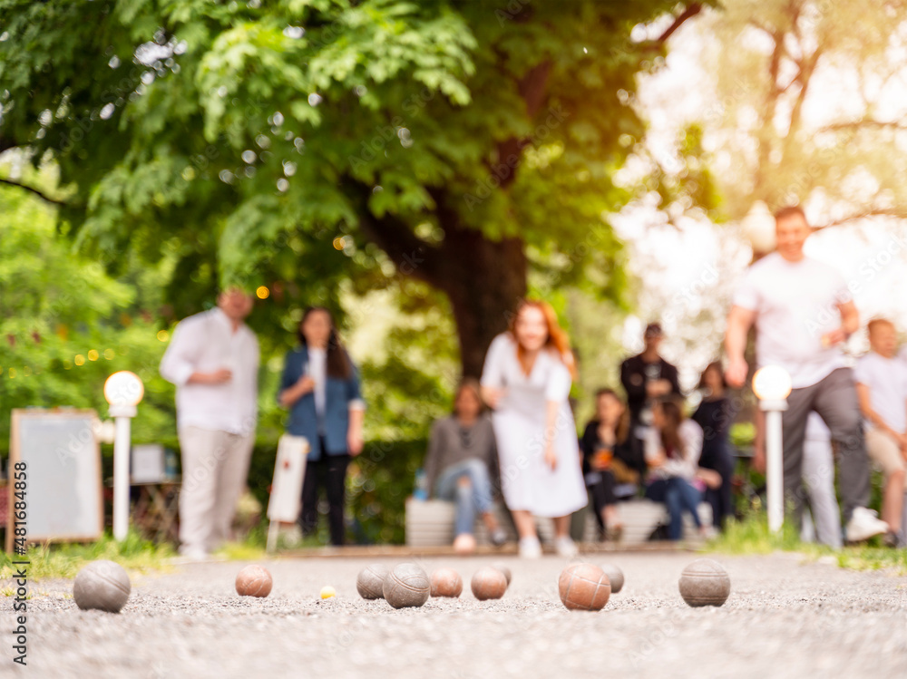 Friends playing bocce game woman through a ball above green trees park ...