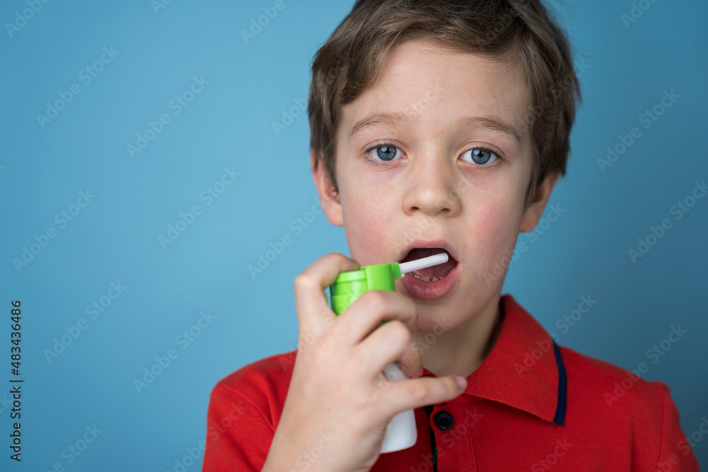 Caucasian boy sprays an aerosol into his mouth to treat sore throat ...