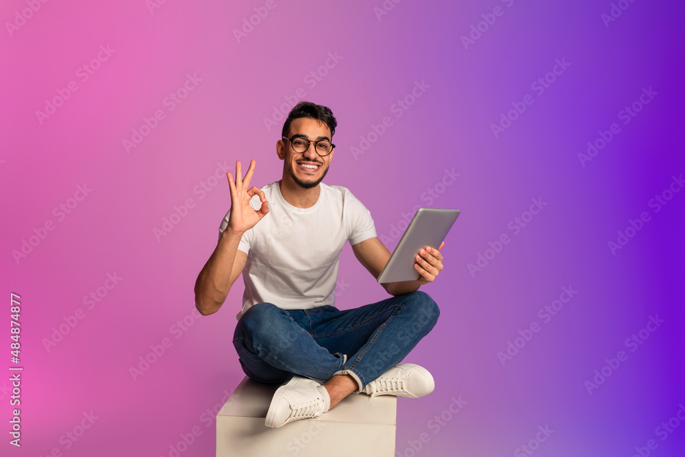 Full length of young Arab guy using tablet pc, showing okay gesture ...