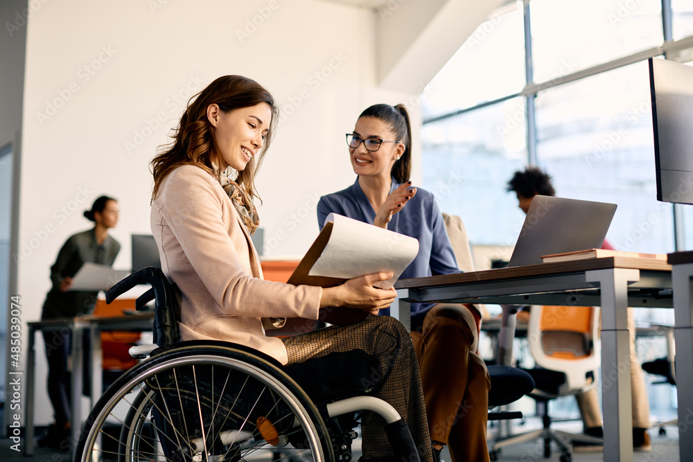 Happy businesswoman in wheelchair going through reports while working ...