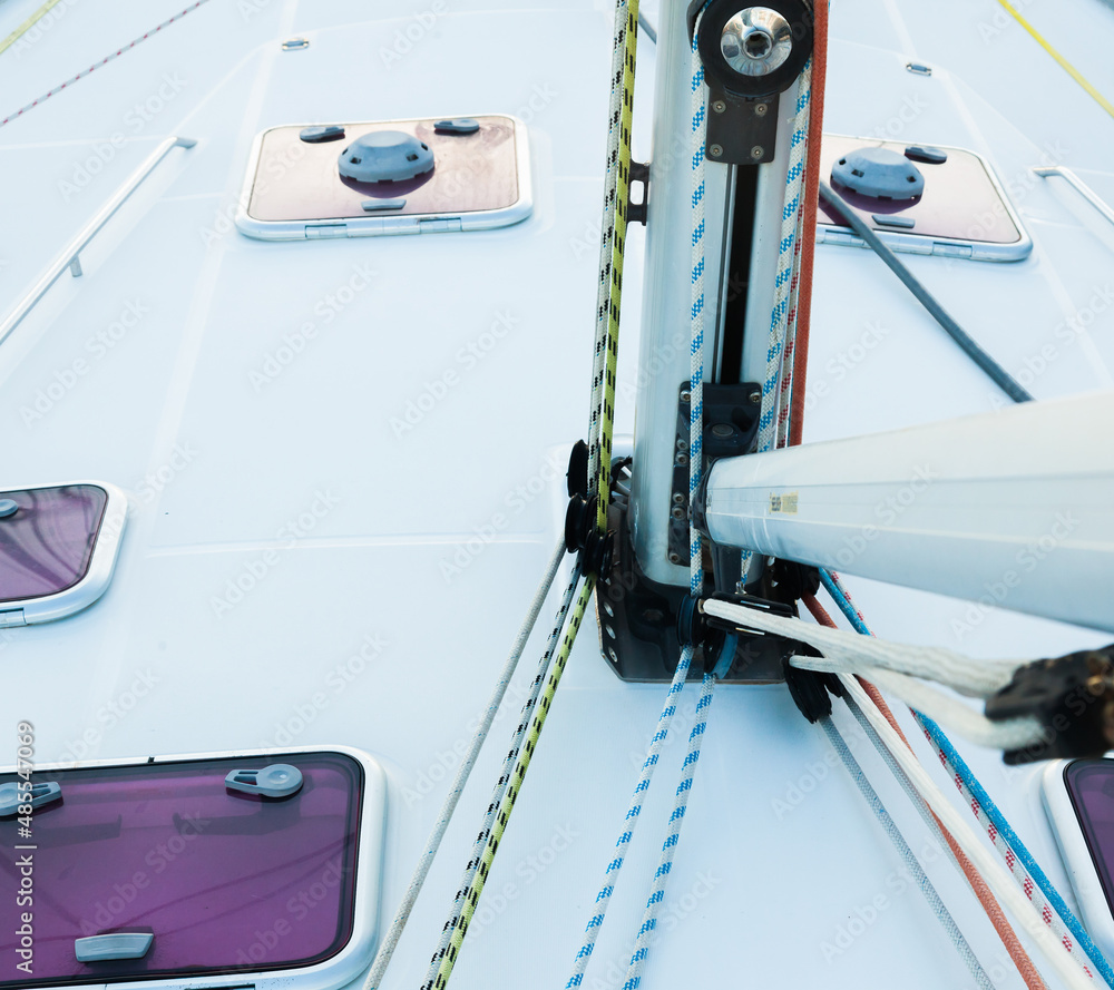Part of the mast and hull of a sailing yacht, with multi-colored ropes, rollers and hinges for ...