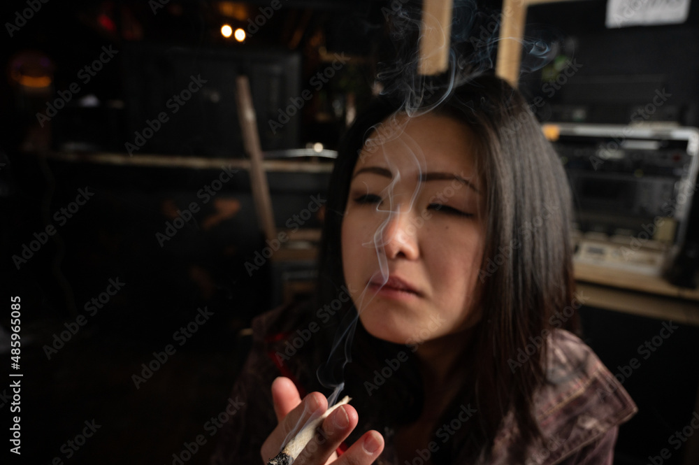 Foto de Stock Asian girl smoking a weed joint getting high inhaling and ...