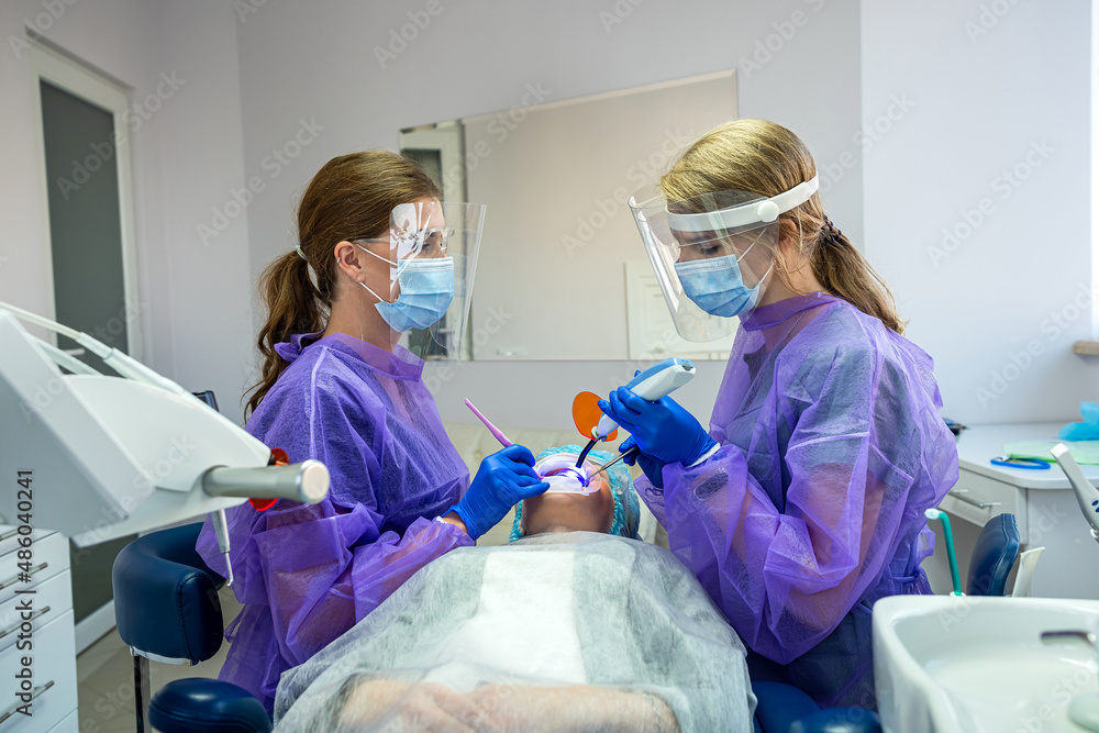 Dentist and assistant in blue latex gloves and masks fill the teeth of ...