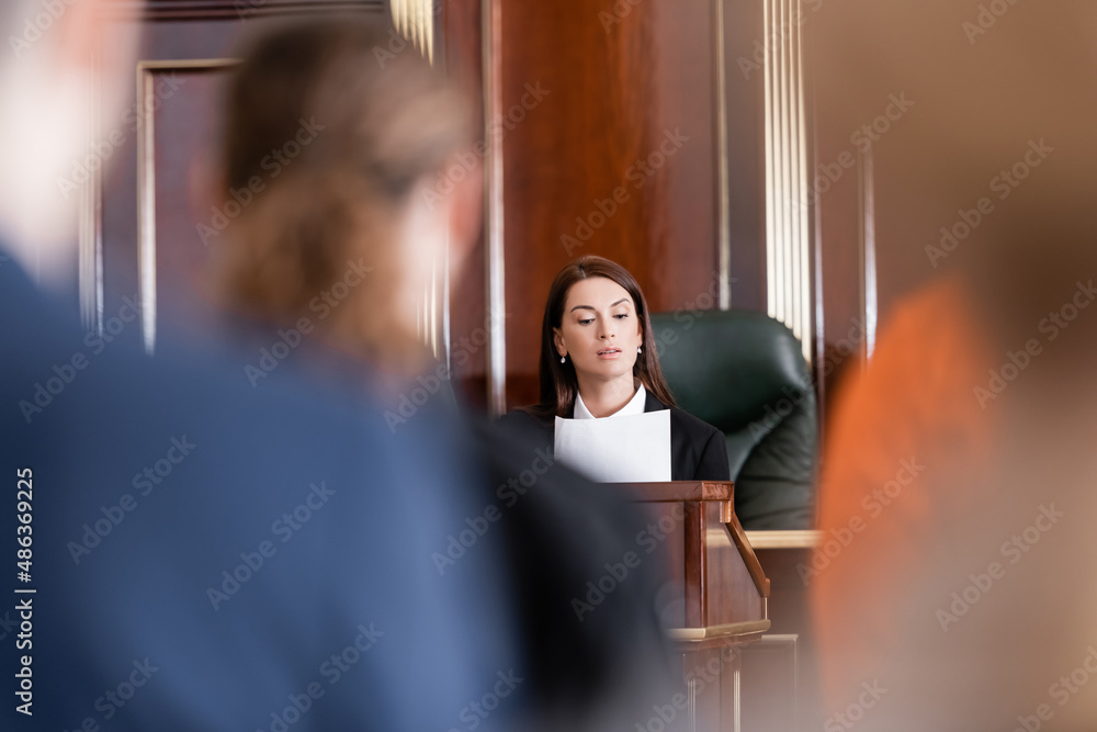 prosecutor reading lawsuit in court near people on blurred foreground ...