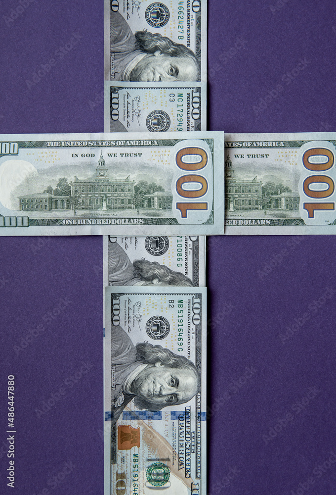 cross folded from one hundred dollar bills on a purple background ...