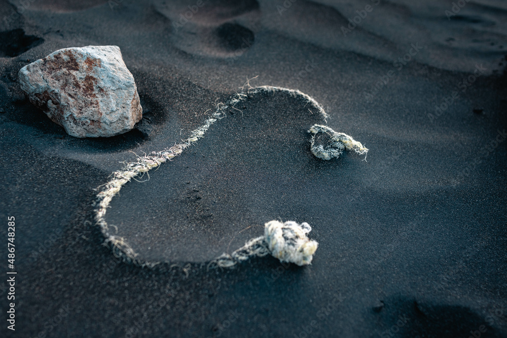 Piece of boat rope half buried on a black sand beach. Pollution of the ...