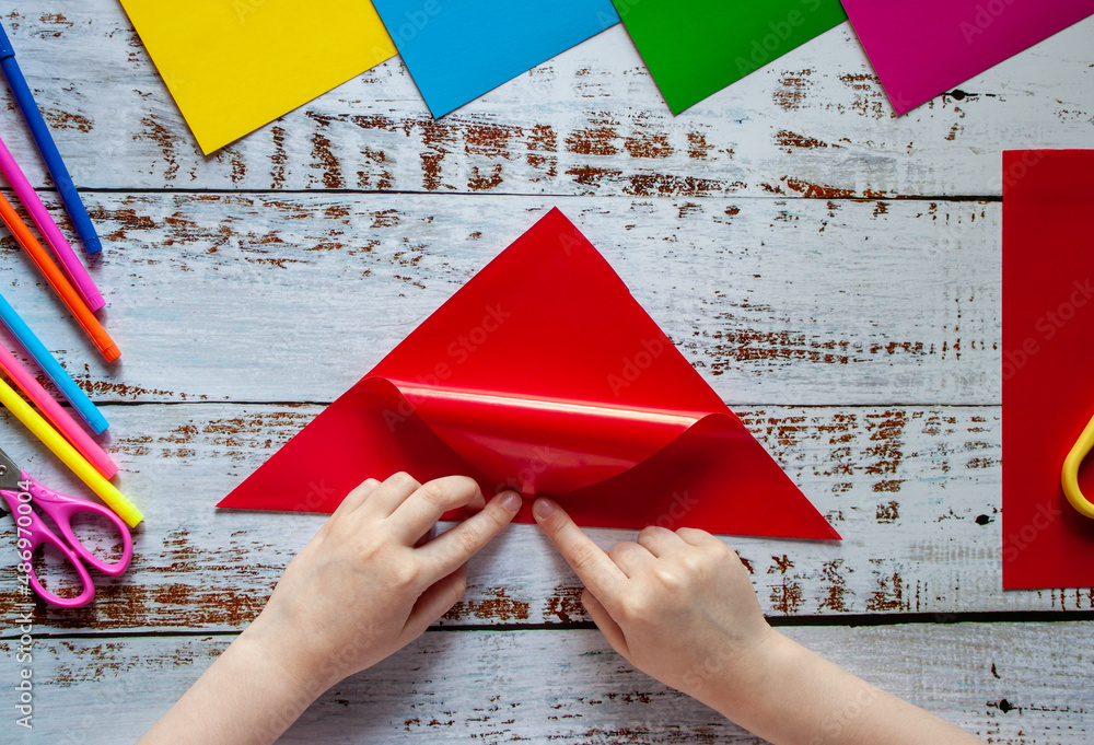 The hands of a child making origami from colored red paper, top view ...