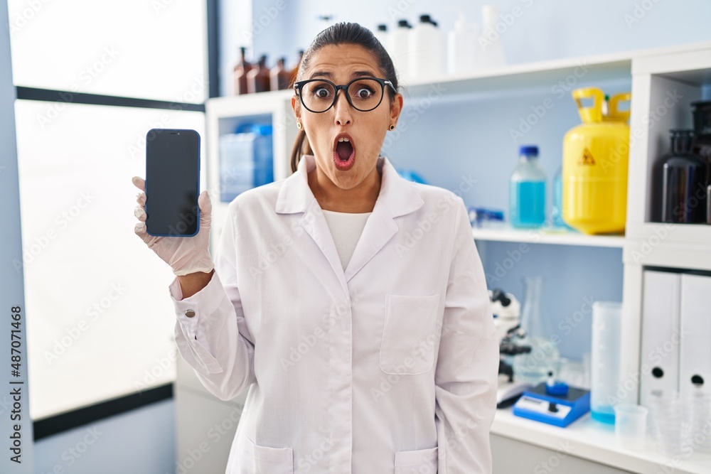 Young hispanic woman working at scientist laboratory with smartphone ...