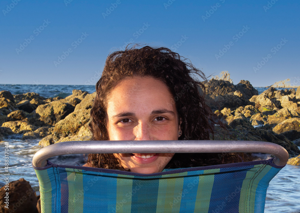 Young brunette woman leaning on the back of a beach chair with colored ...