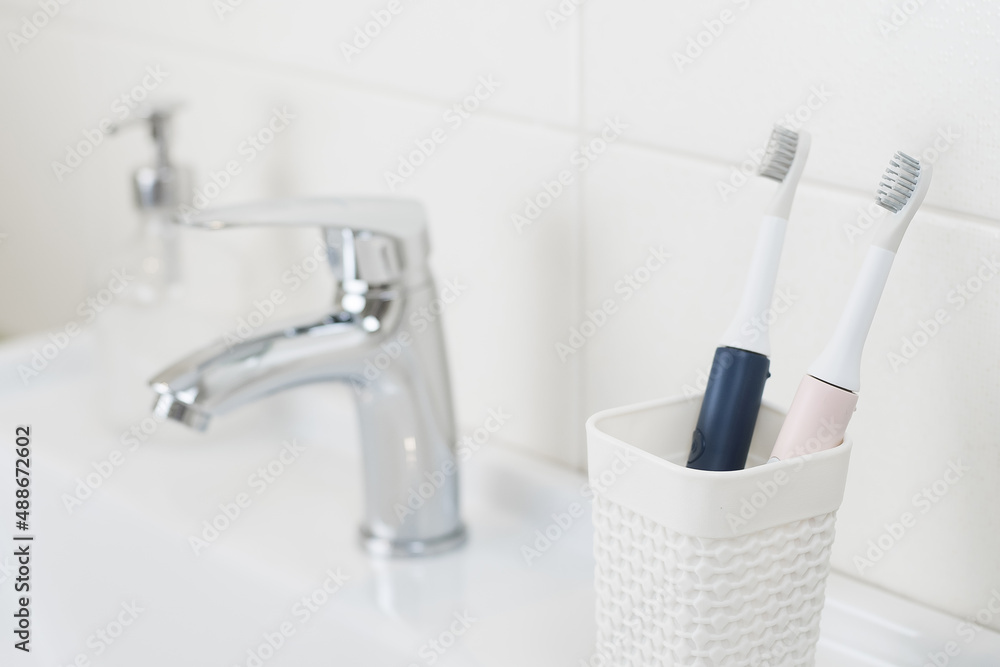 New modern ultrasonic toothbrushes in a glass on the bathroom sink. Jaw ...