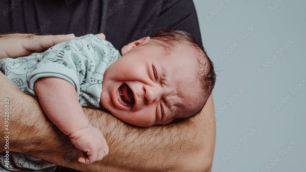newborn on his father's arm screams crying with expression of suffering ...