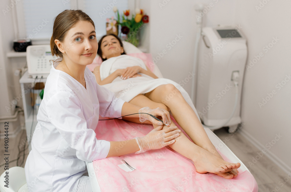 Dermatologist doing hair removal treatment on patient's leg with ...
