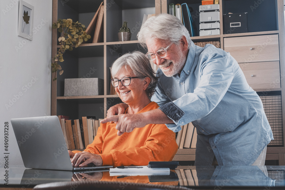Elderly man and woman having fun using laptop at home office. Smiling ...