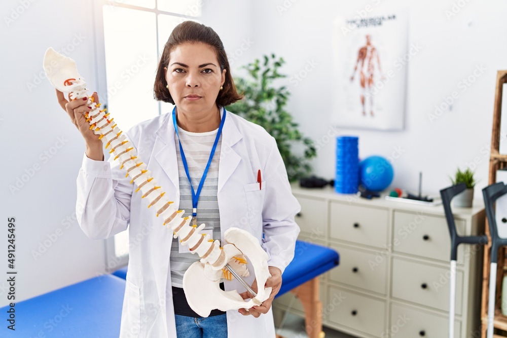 Middle age hispanic physiotherapy woman holding anatomical model of ...