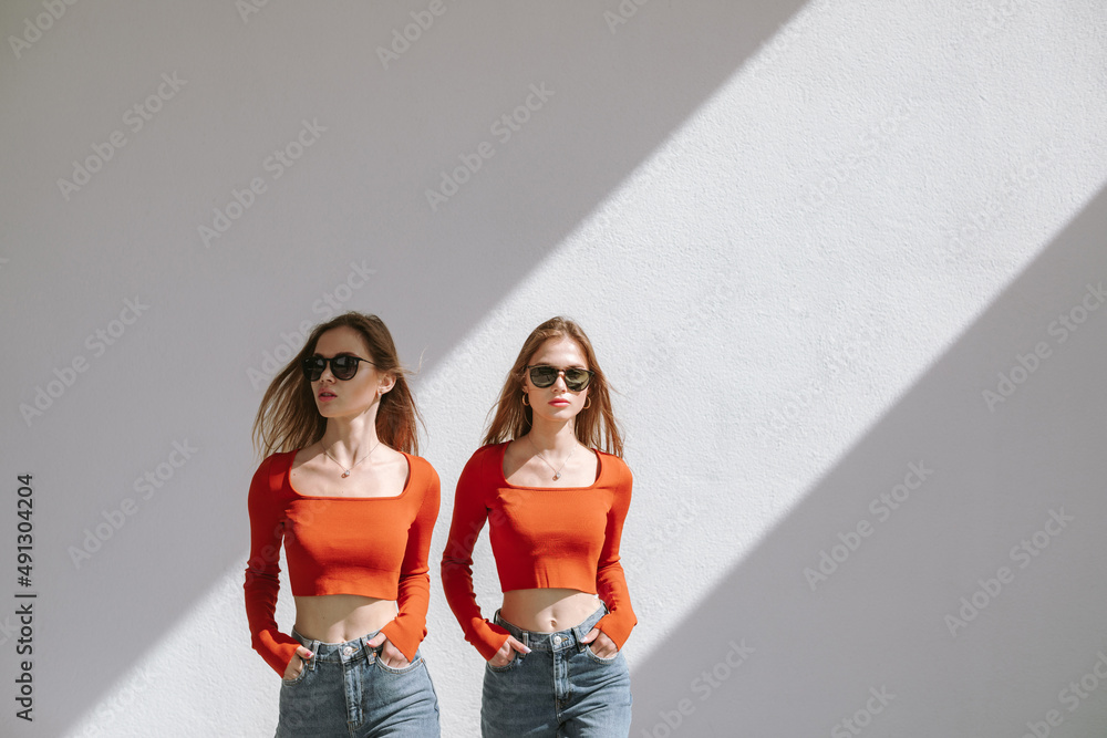 Two sensual young twin sisters in sunglasses and identical clothes ...