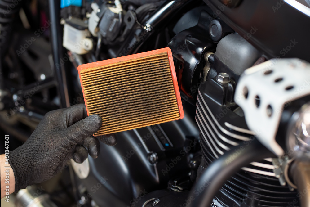 mechanic holding dirty Engine Air Filter over motorcycle, working in ...