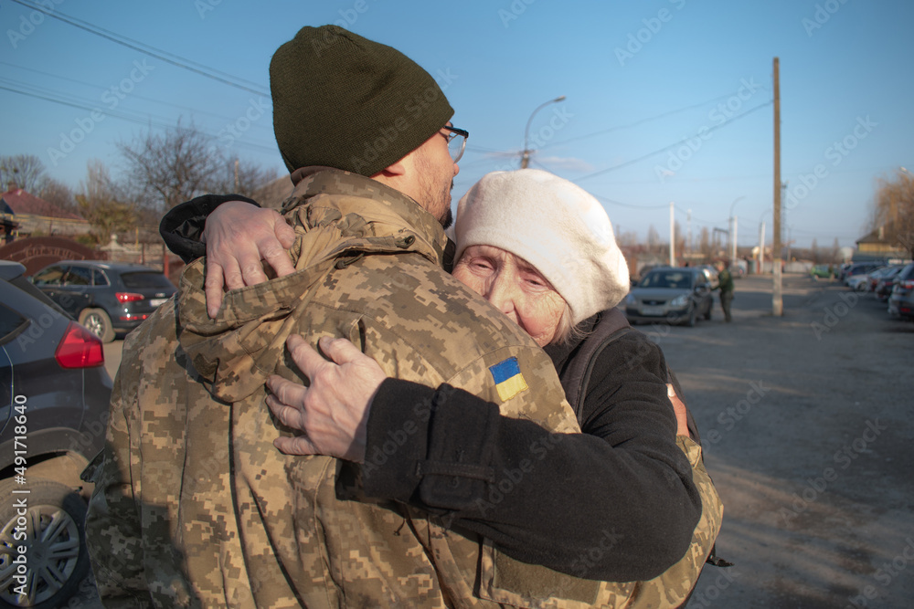 Fotografie Elderly mother says goodbye to her military son. Mom hugs a ...