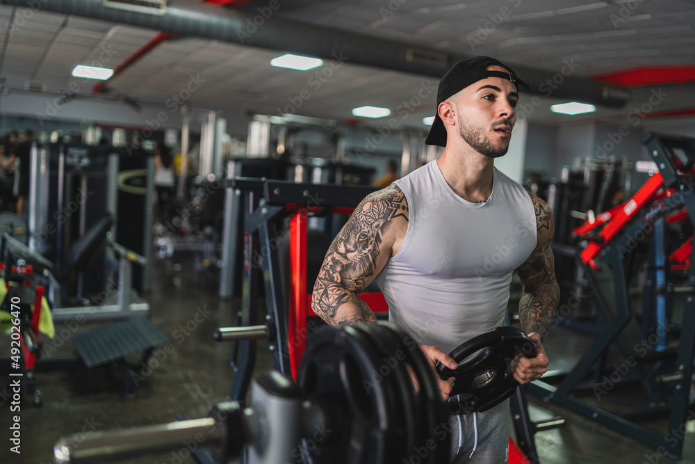 Chico joven musculoso en camiseta de tirantas blanca sujetando una pesa ...