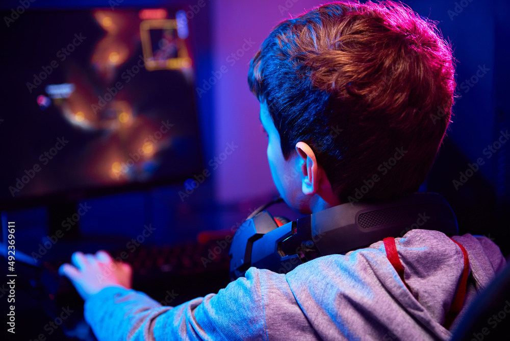 Teenager boy play computer video game in dark room, use neon colored ...