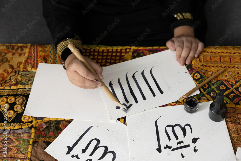 close up muslim girl hands writing Arabic text with bamboo pens and ...