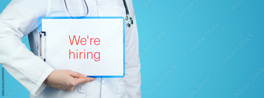 We're hiring. Doctor with stethoscope holds blue clipboard. Text is ...