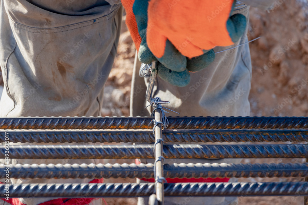 A worker uses steel tying wire to fasten steel rods to reinforcement ...