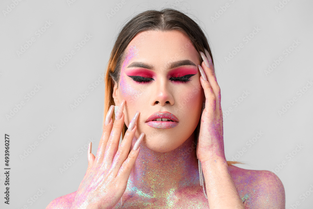 Fashionable young transgender woman with glitters on body against light ...