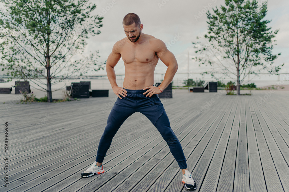 Athlete guy does sport exercises in fresh air, stands with naked torso ...