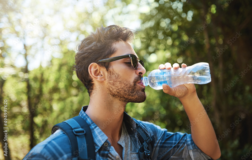 Staying hydrated on his hike. Shot of a young man stopping for a drink ...
