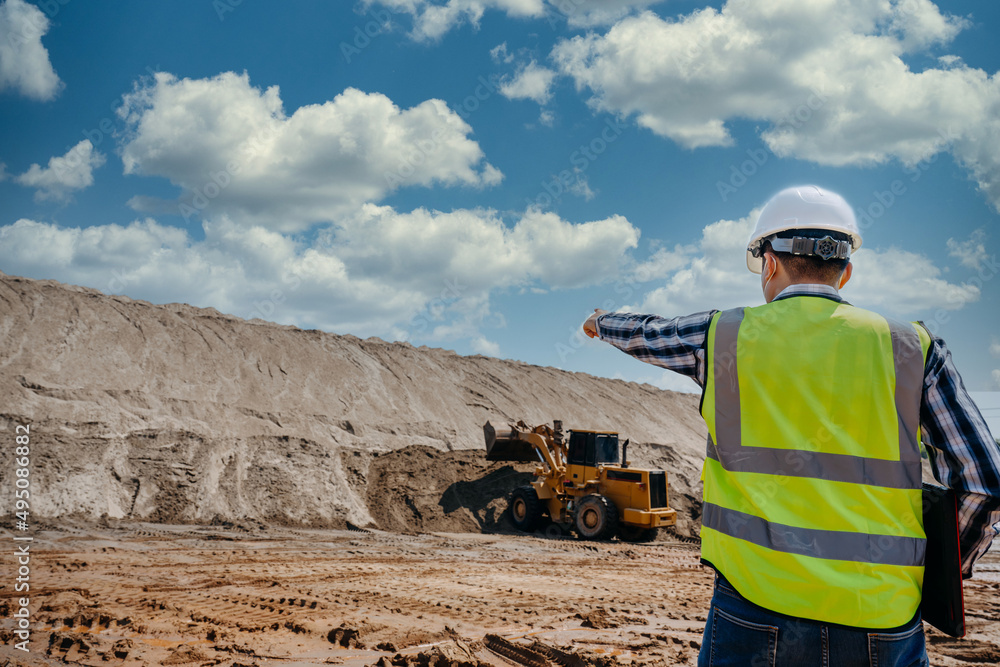 A young man civil engineer working at sand quarry inspects the ...