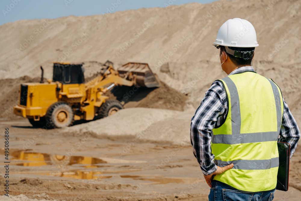 A young man civil engineer working at sand quarry inspects the ...