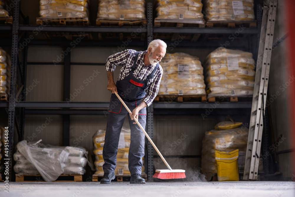 A senior factory worker is brooming factory hall. Stock Photo | Adobe Stock