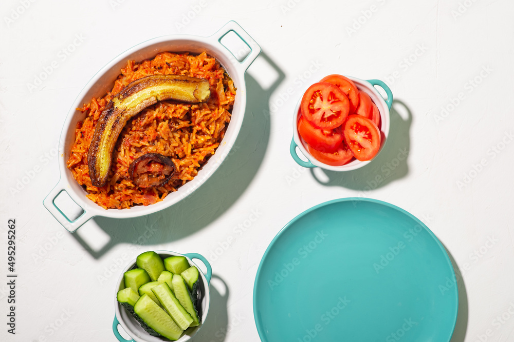 Jollof rice with fried banana. Fresh vegetables - tomato and cucumber ...