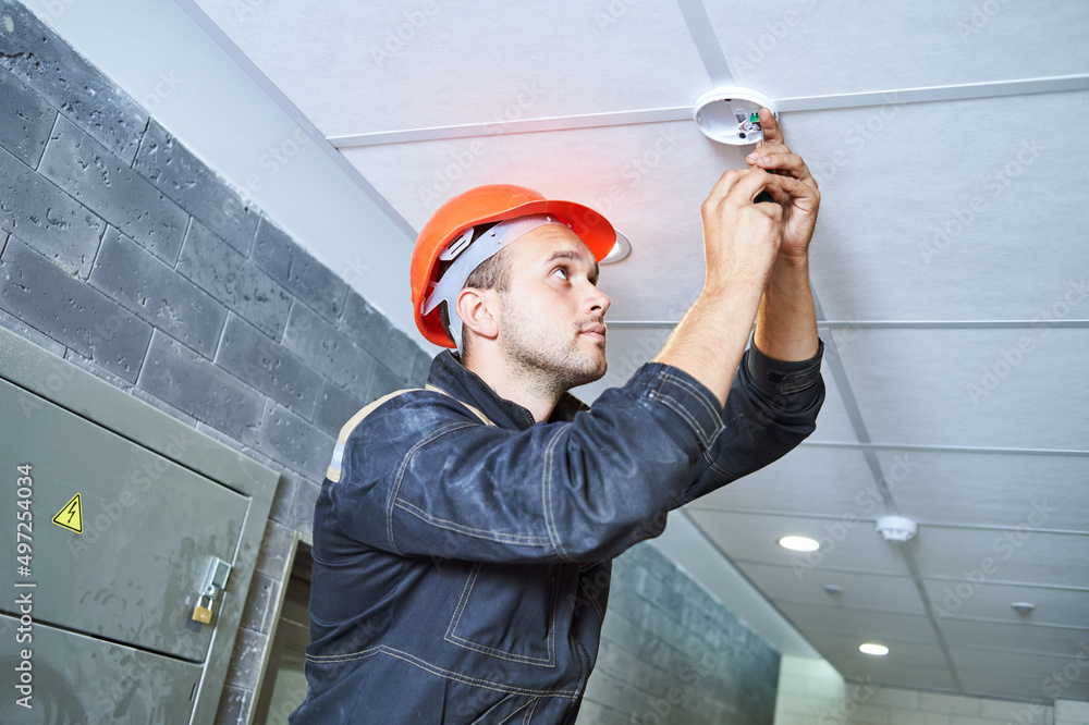 worker installing smoke detector on the ceiling. Fire alarm system ...