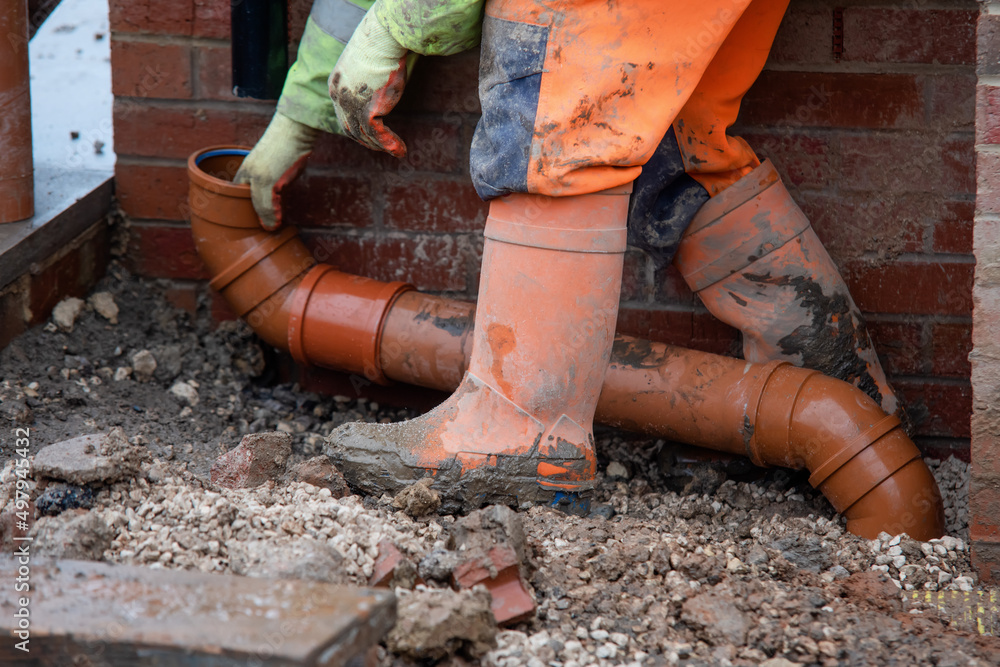 Groundworker fitting plastic drainage pipe to connect down pipe from ...