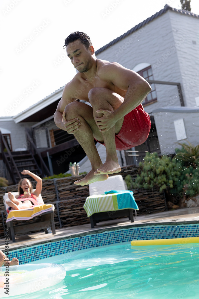 Full length of shirtless biracial man jumping in swimming pool while ...