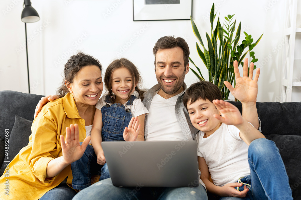 Virtual meeting. Family of four waving to screen while using laptop for ...