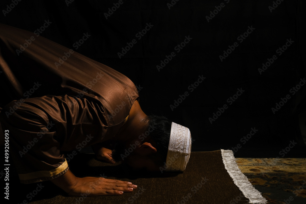 A picture of men perform "sujud" on praying mat during at night. Sign ...