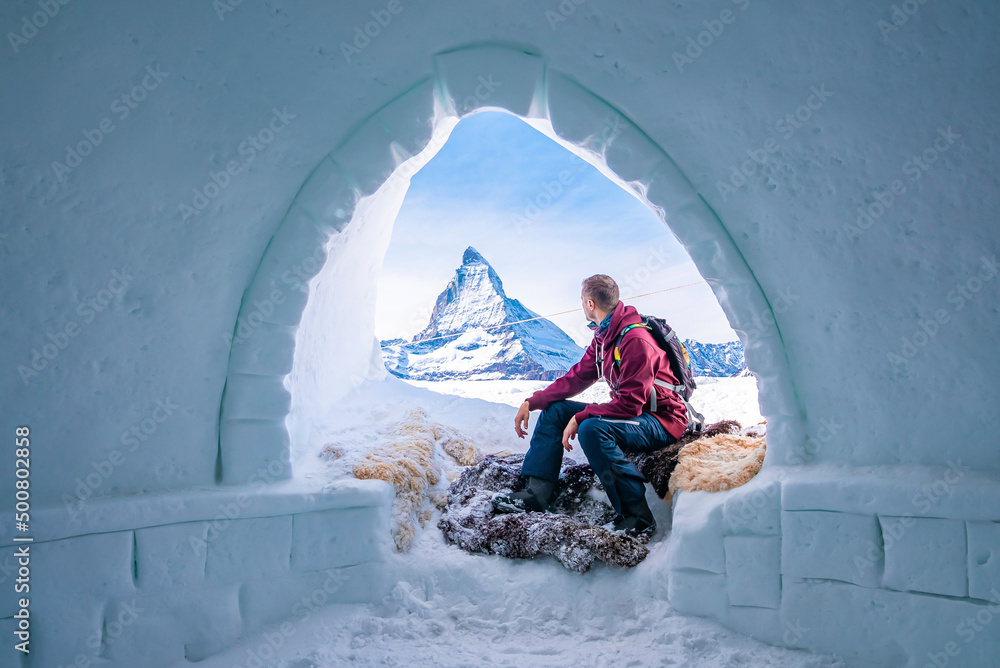 Male tourist sitting in entrance of igloo. Young man is looking at ...