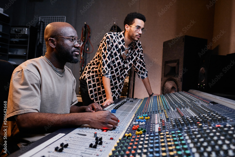 Modern mature Black sound engineer and stylish young singer working on ...