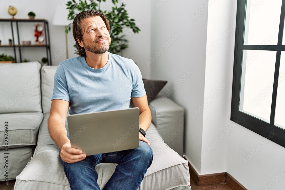 Handsome middle age man using computer laptop on the sofa smiling ...