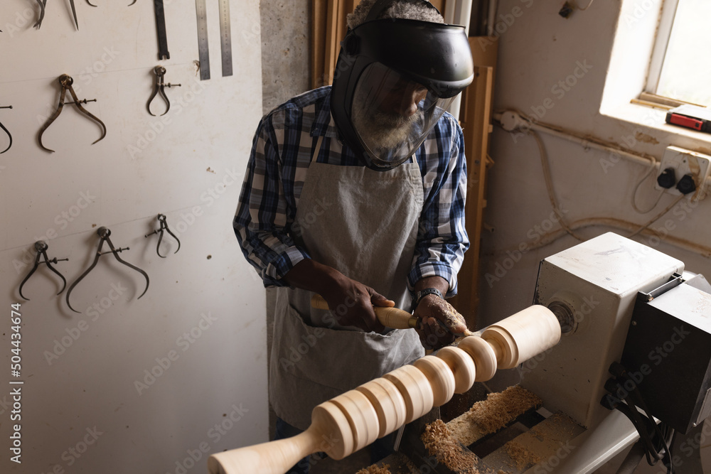 African american mature carpenter in safety face shield shaping and ...