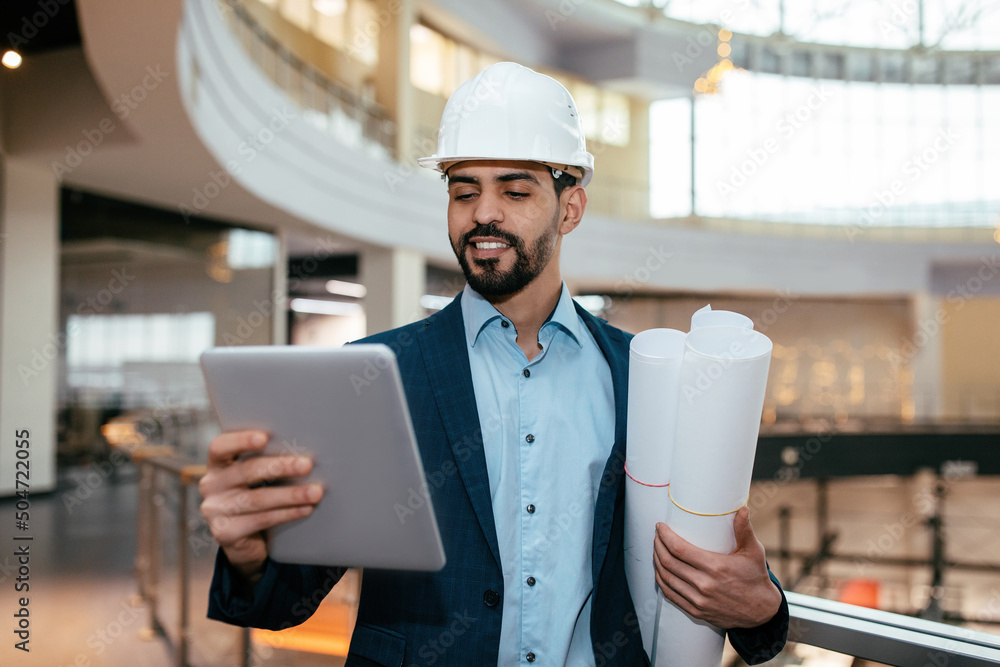 Smiling attractive young arab man engineer with beard in hard hat ...